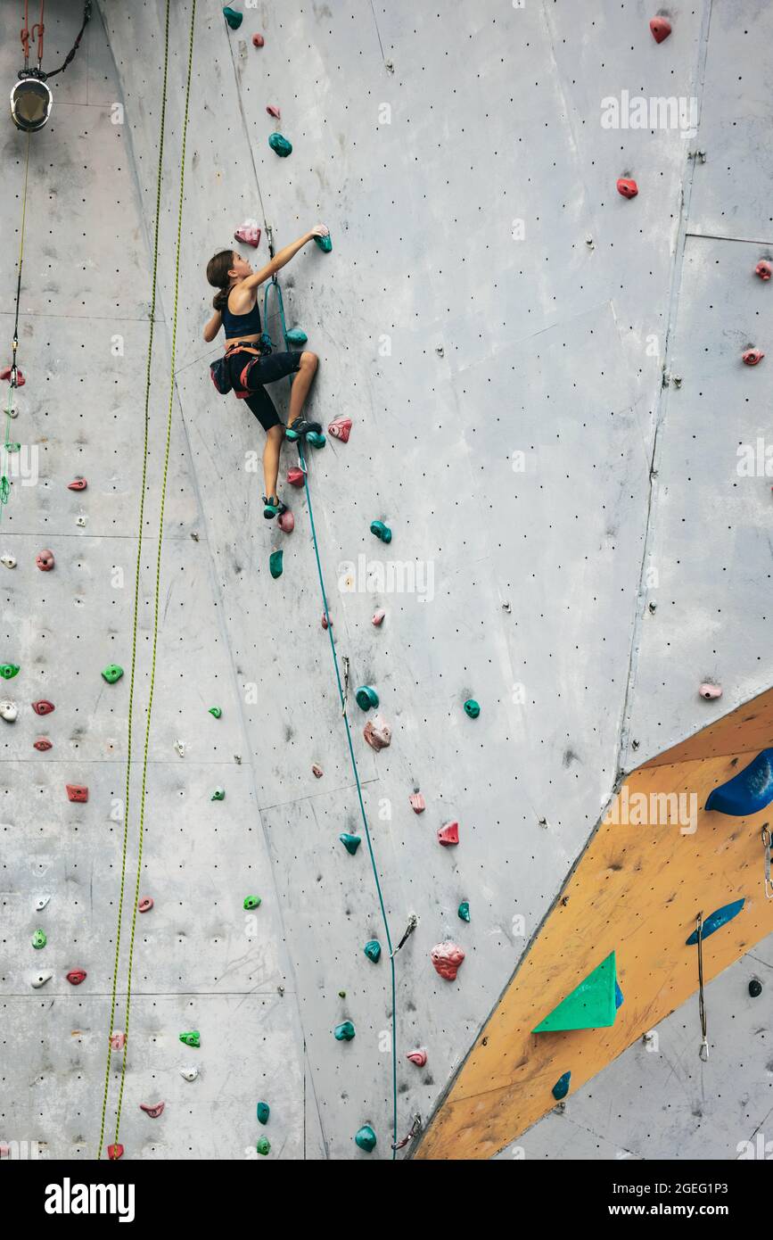 One cute teen girl with climbing equipment practicing on rock wall ...