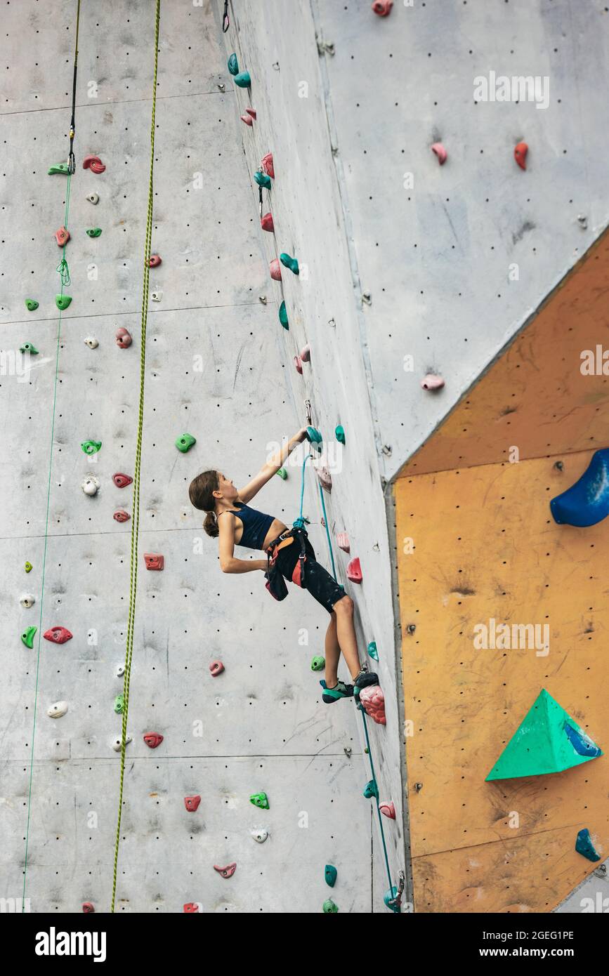 One cute teen girl with climbing equipment practicing on rock wall ...