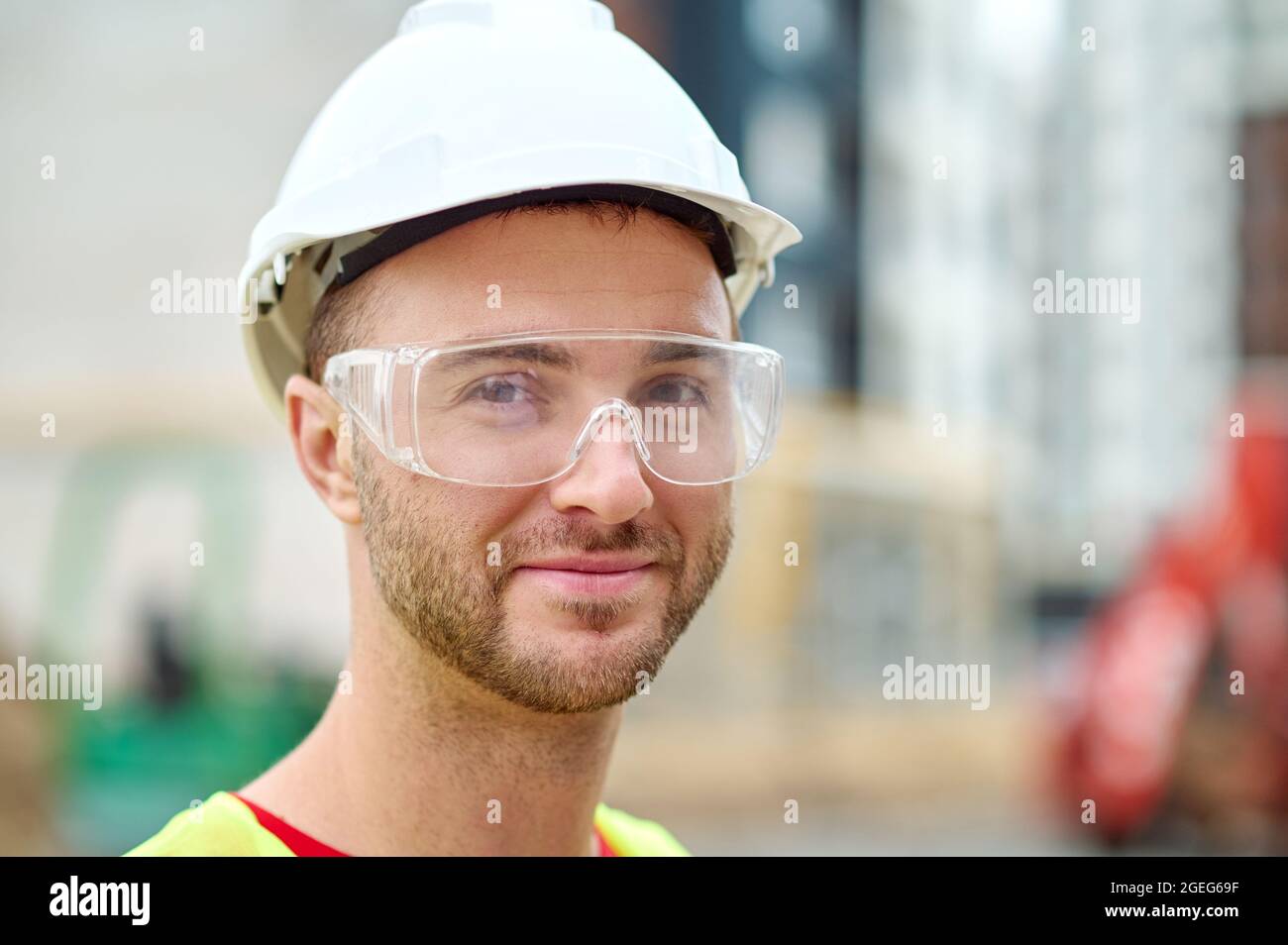 Pleased attractive builder in safety goggles posing for the camera ...