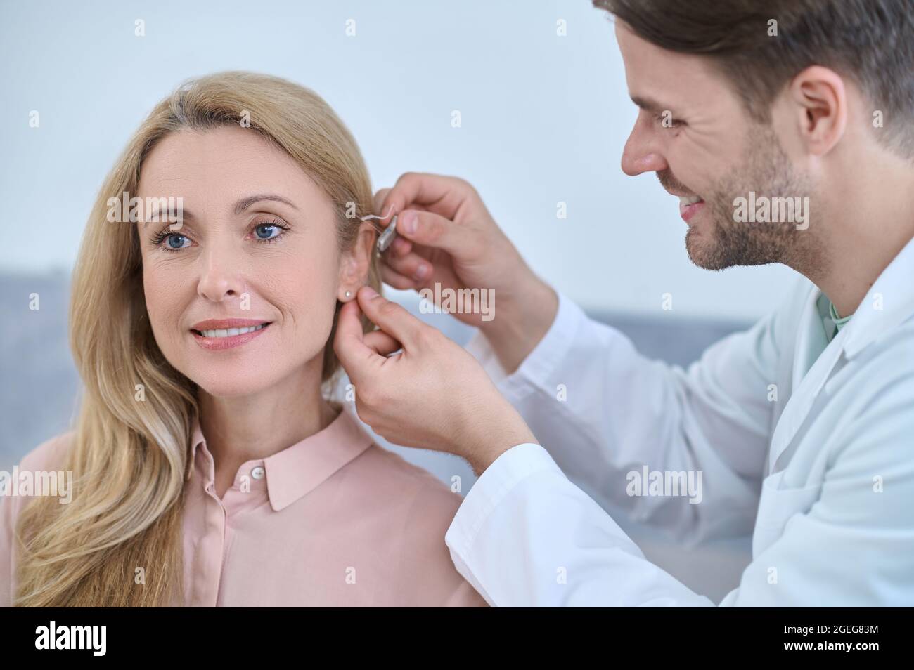 Joyous pleasant doctor fixing a deaf aid behind the womans ear Stock ...