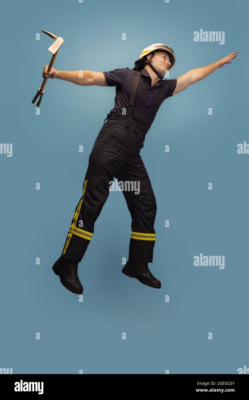 Vertical portrait of young male fireman in uniform posing with hatchet ...