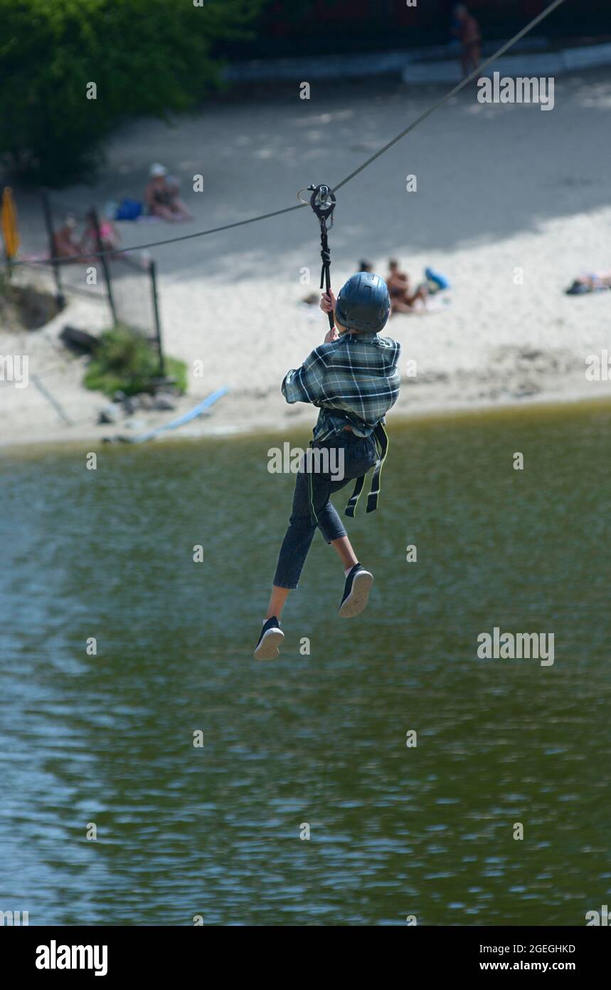 Little girl descending on the rope swing over the river, back view ...