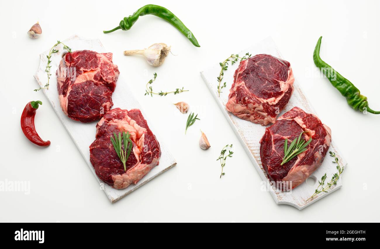 raw piece of beef ribeye with rosemary, thyme on a white table, top ...