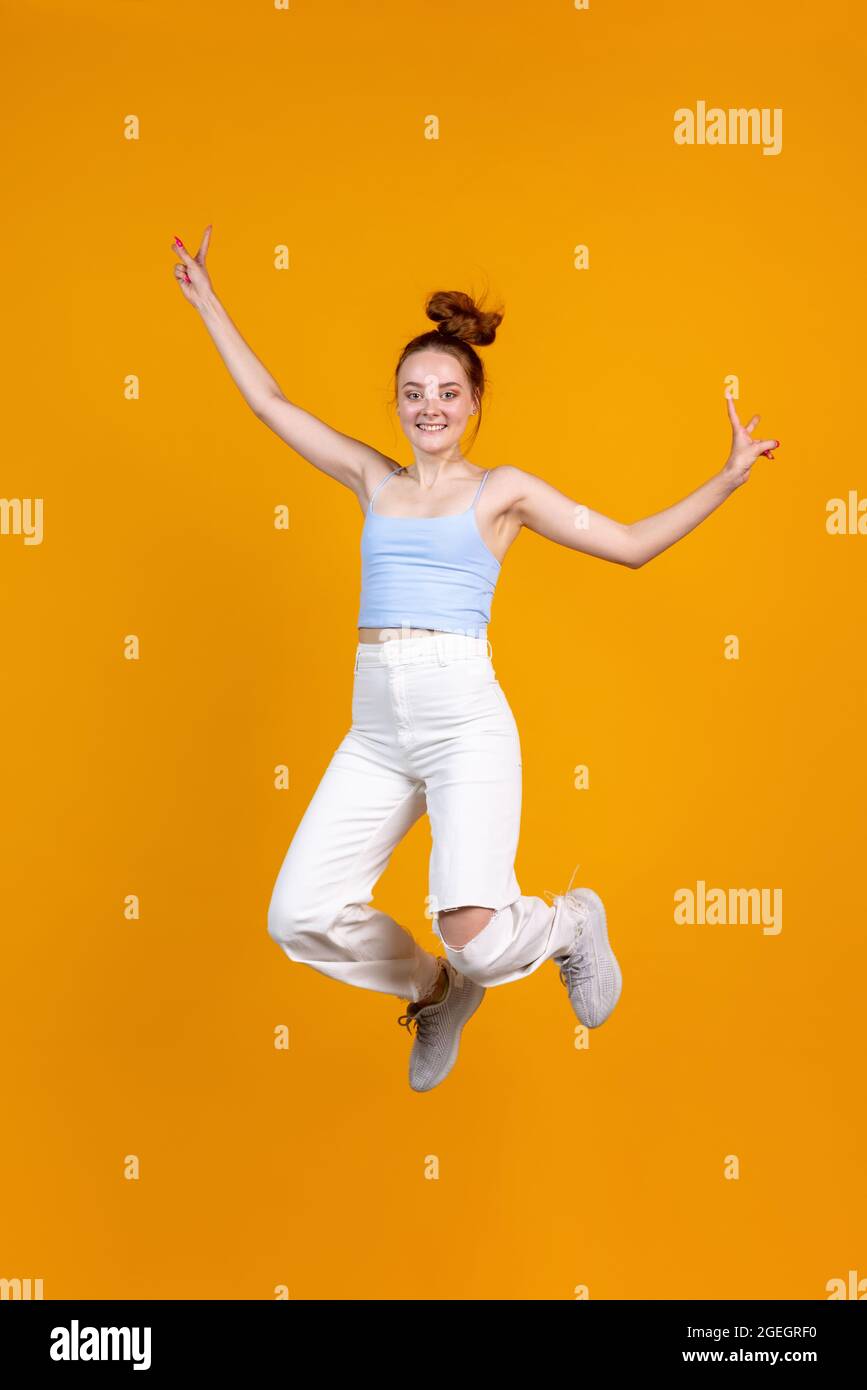 Vertical image of young cute girl jumping isolated on yellow studio ...