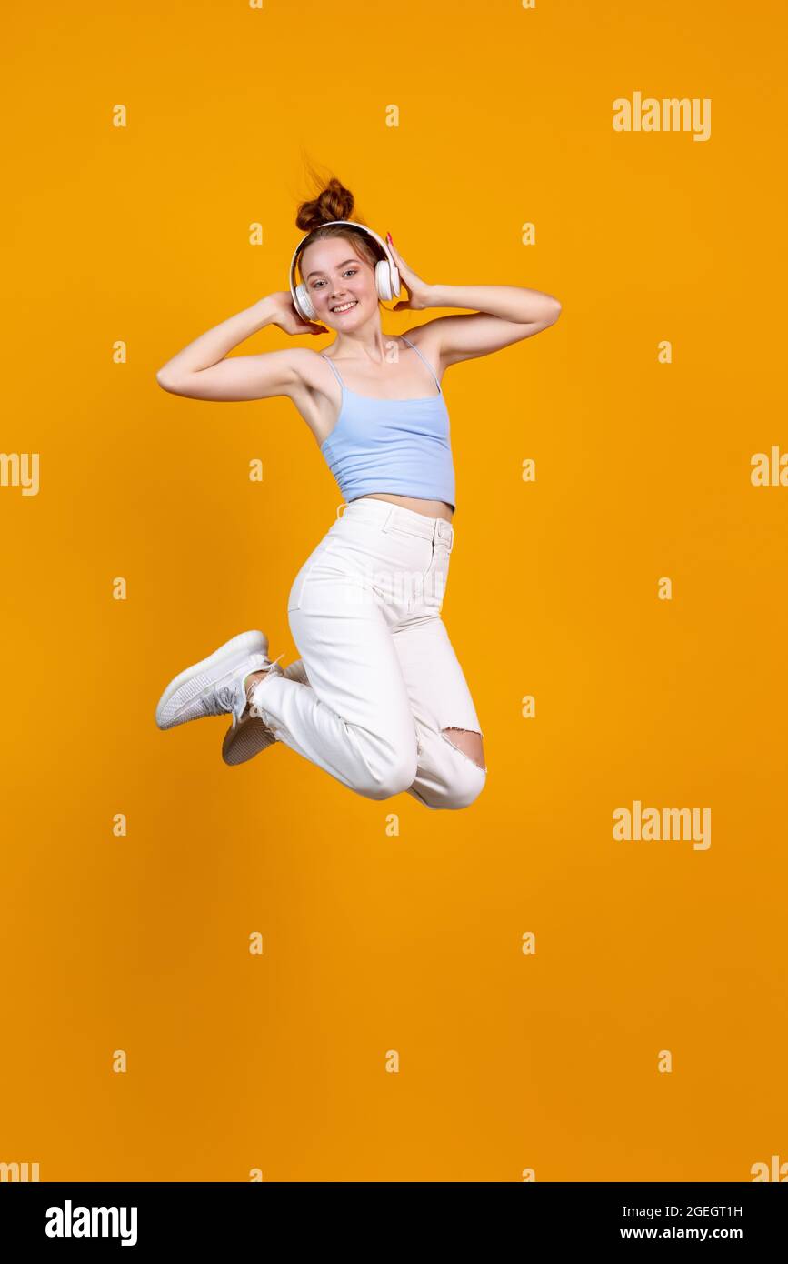 Vertical image of young cute girl jumping isolated on yellow studio ...