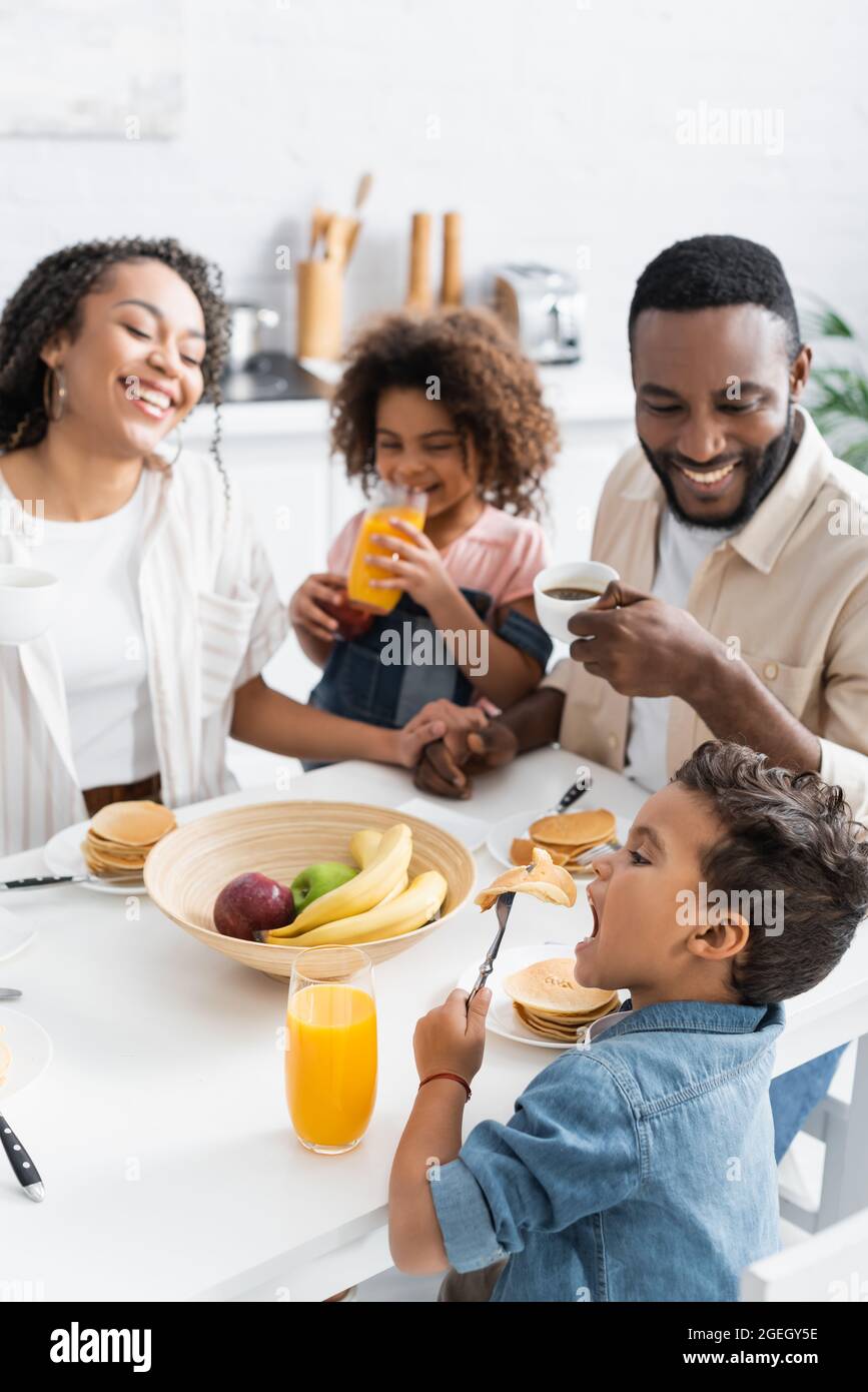 african american boy eating pancakes near happy parents and sister ...