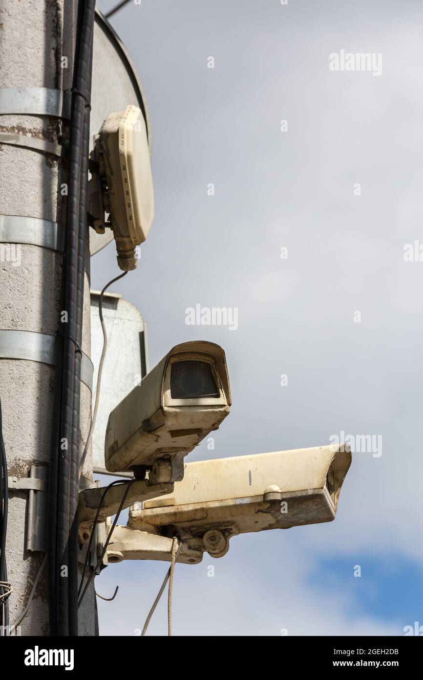 two old security surveillance cameras on street light pole on blue sky ...