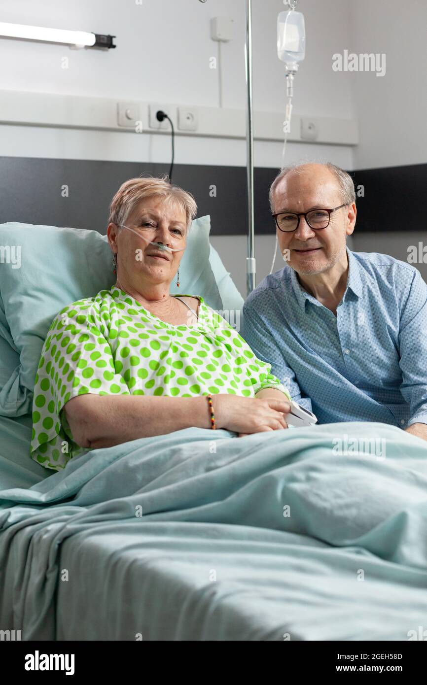 Retired hospitalized sick woman lying in bed with husband visitor ...