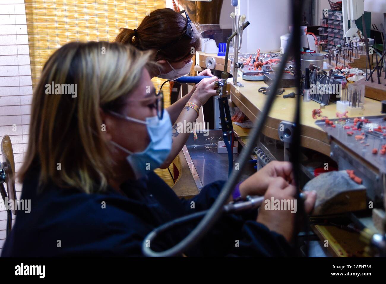 Women wearing masks learn coral processing techniques inside a ...