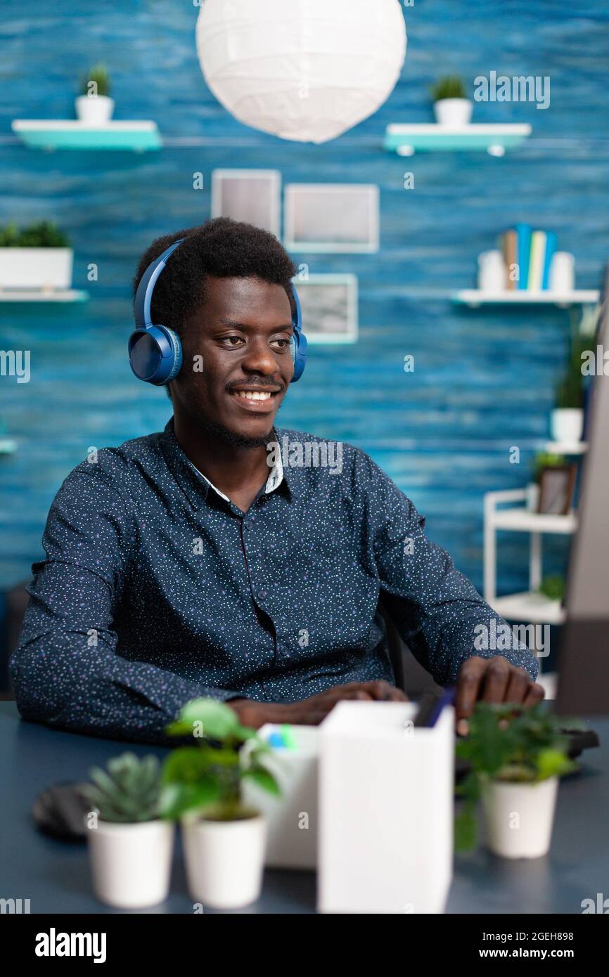Smiling african american man using laptop with headphones working from ...