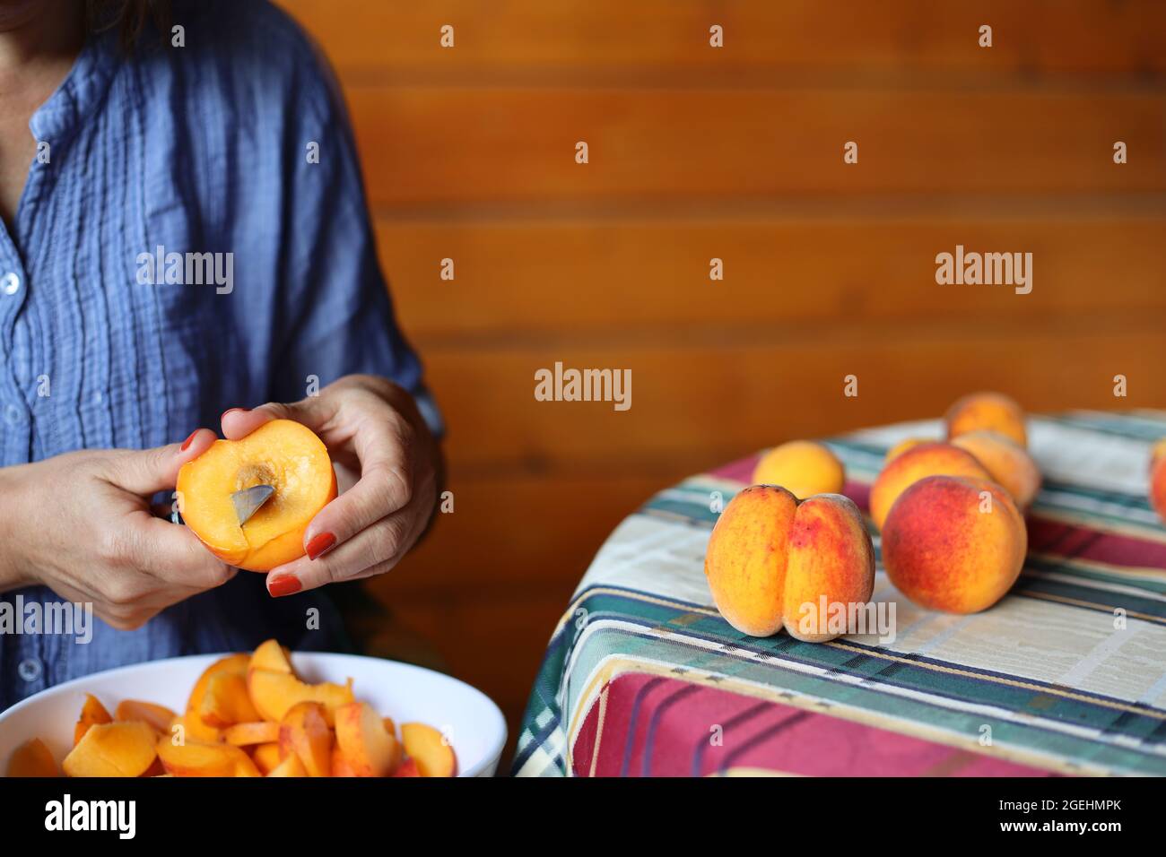 Female hands cutting fresh sweet peaches to make peach jam. A woman is ...