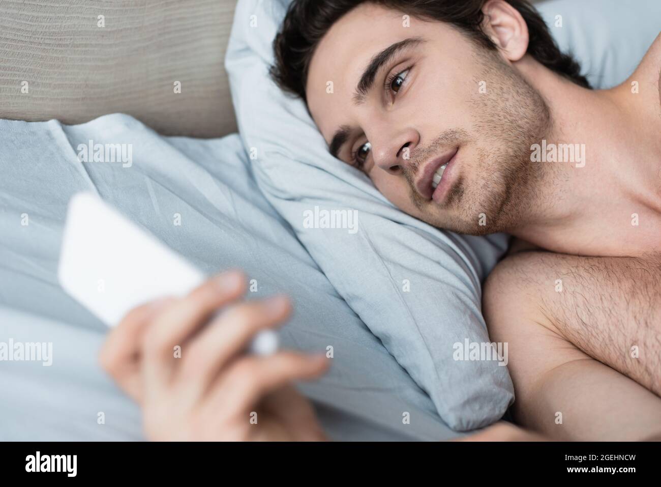 man lying in bed and using blurred mobile phone Stock Photo - Alamy