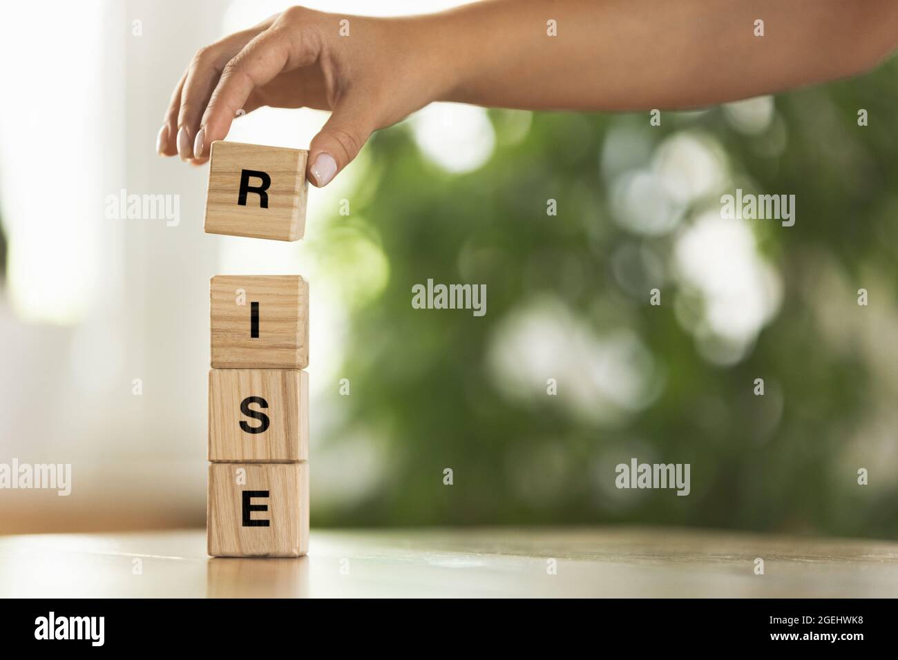 Female hand builds tower of wooden cubes, blocks with word RISE ...