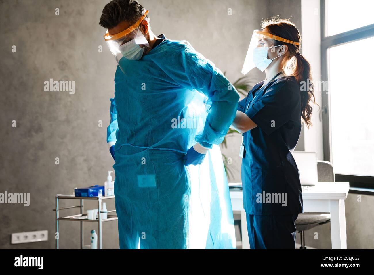 Two medical workers dressing up in uniform standing indoors, wearing ...