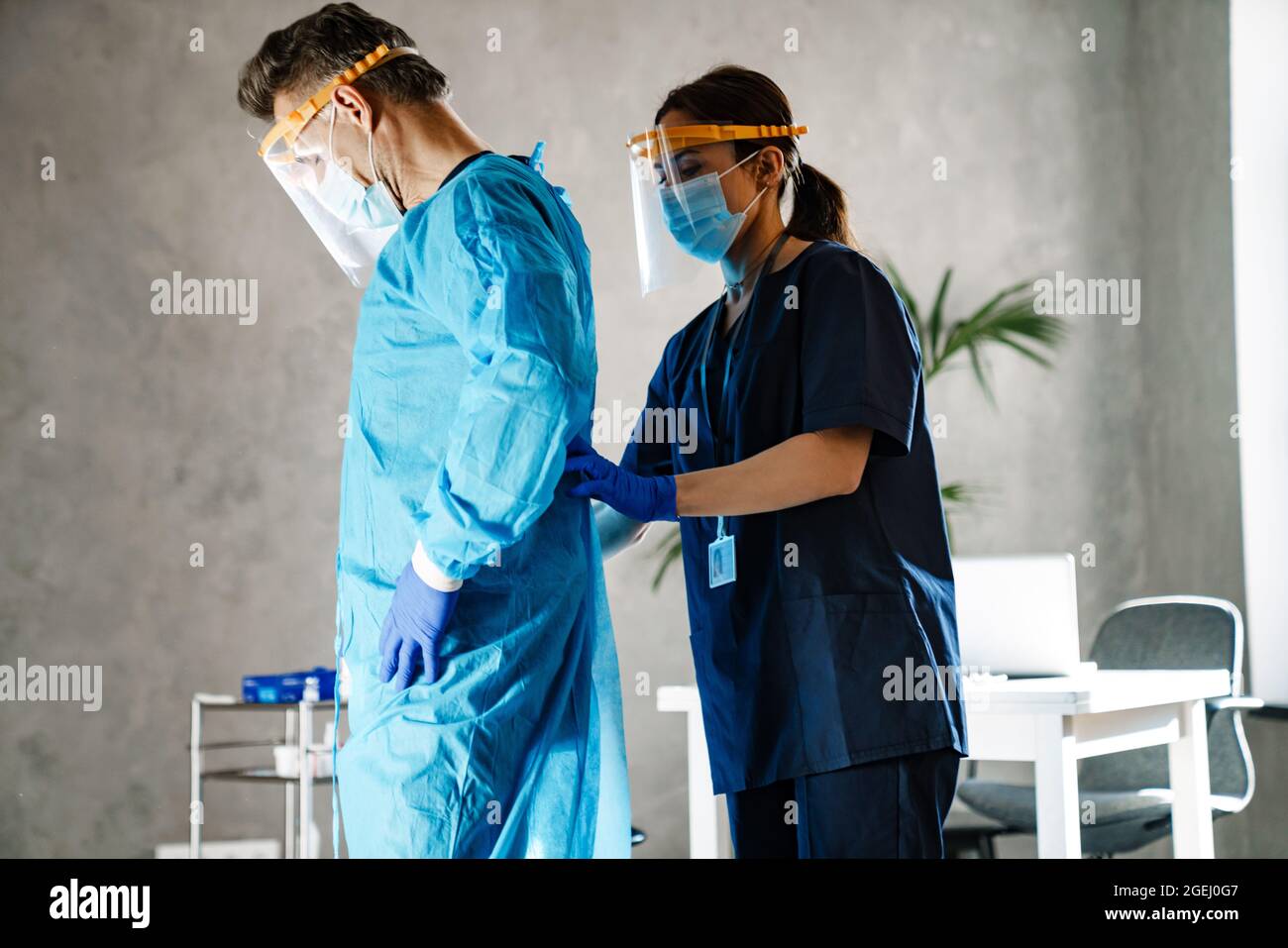 Two medical workers dressing up in uniform standing indoors, wearing ...