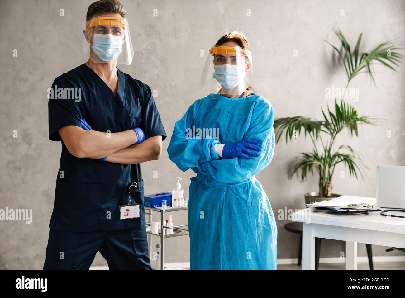 Two medical workers dressed in uniform standing indoors, wearing robes ...