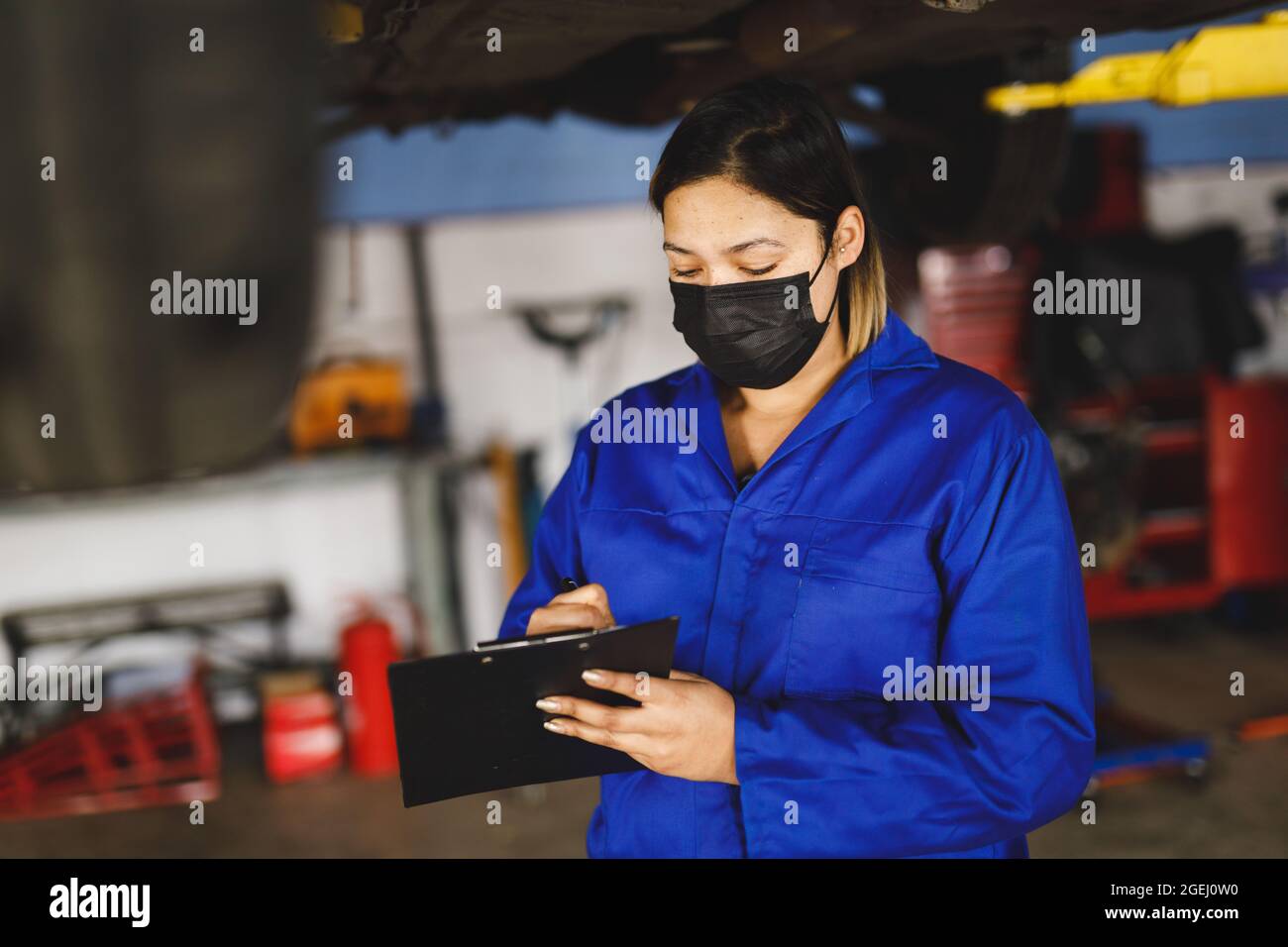 Mixed race female car mechanic wearing face mask and overalls, making ...