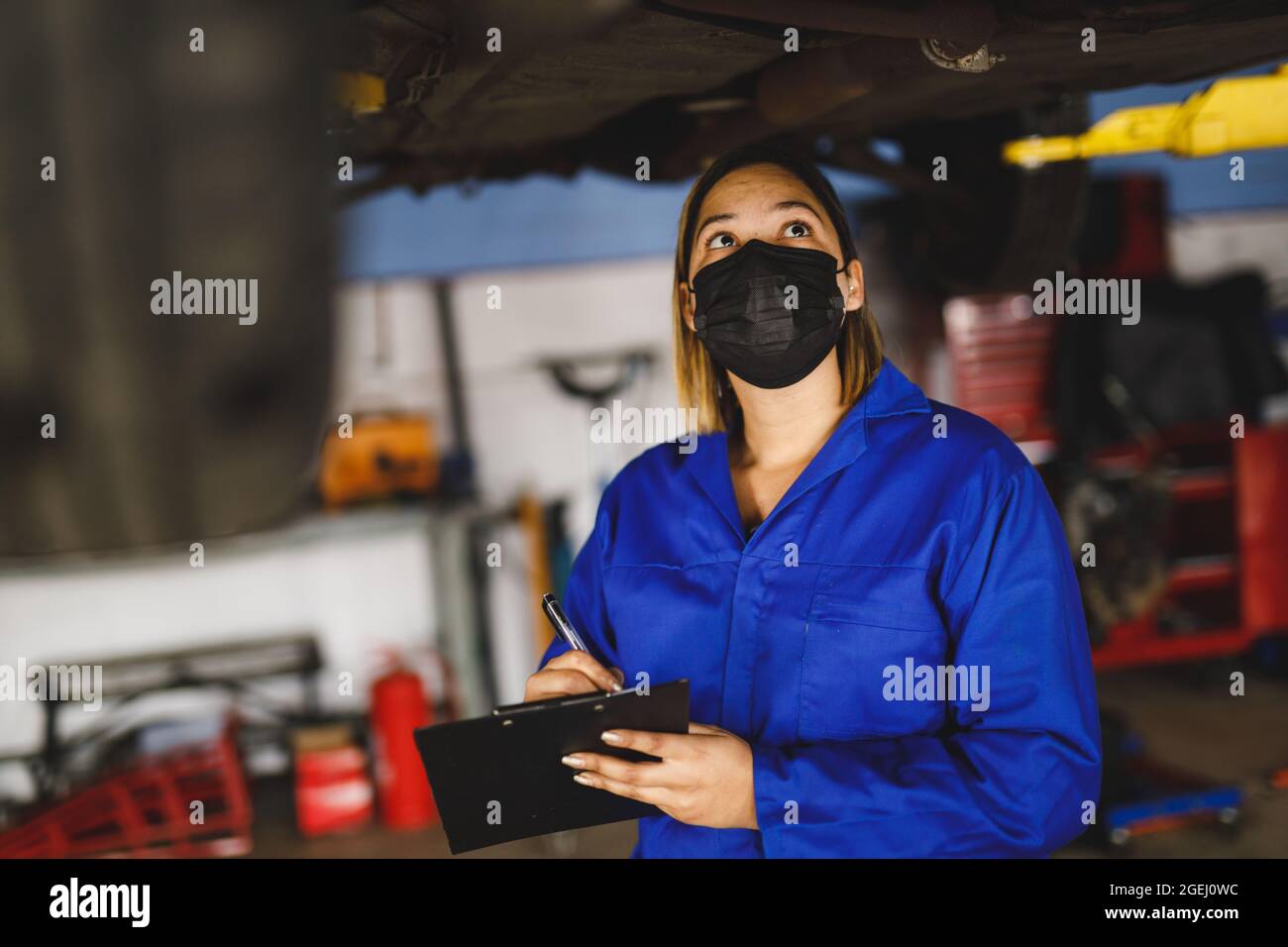 Mixed race female car mechanic wearing face mask and overalls, making ...