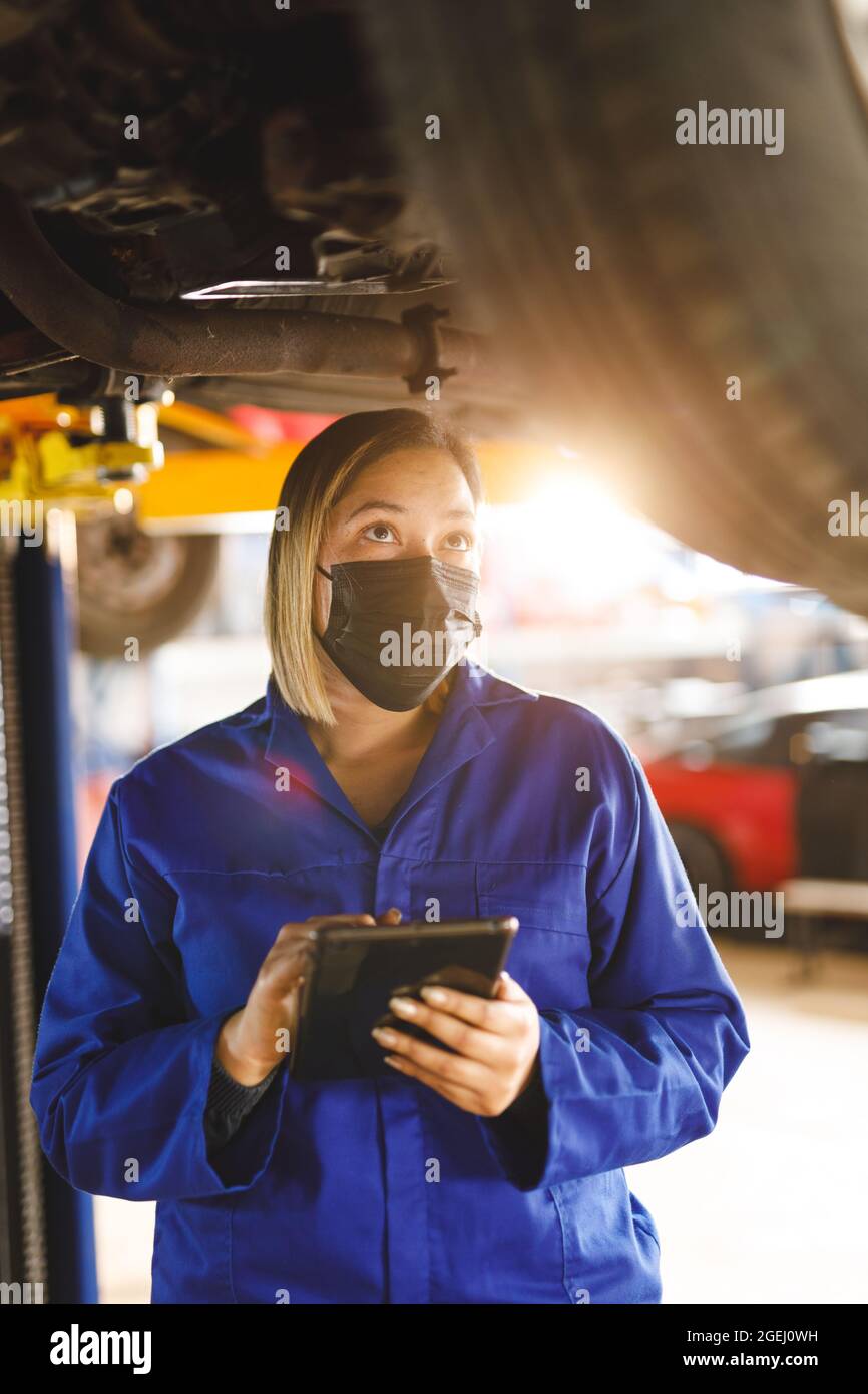 Mixed race female car mechanic wearing face mask and overalls, making ...