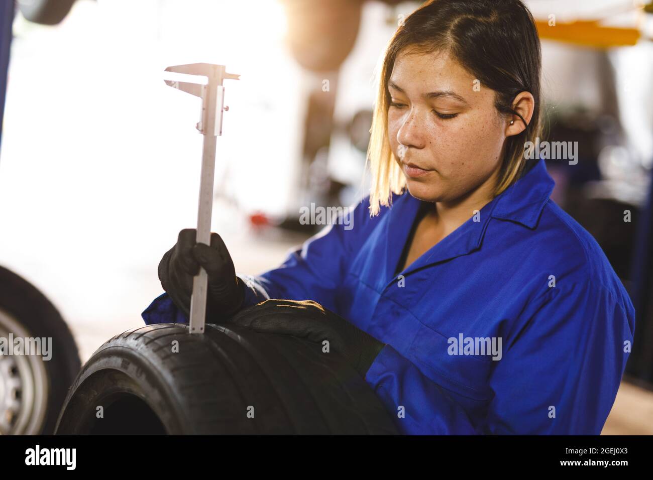 Mixed race female car mechanic wearing overalls, checking tire Stock ...