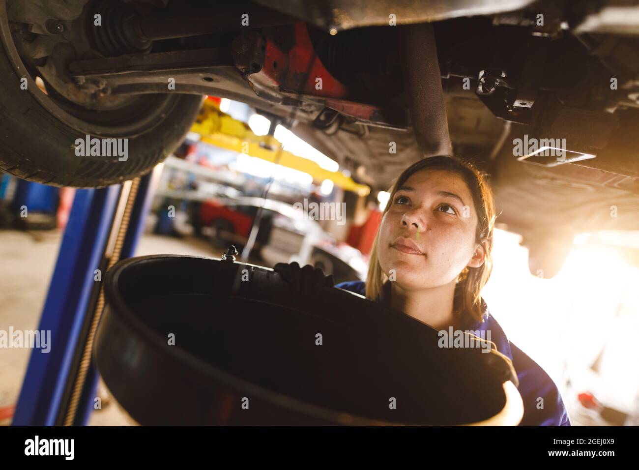 Mixed race female car mechanic wearing overalls, replacing car oil ...