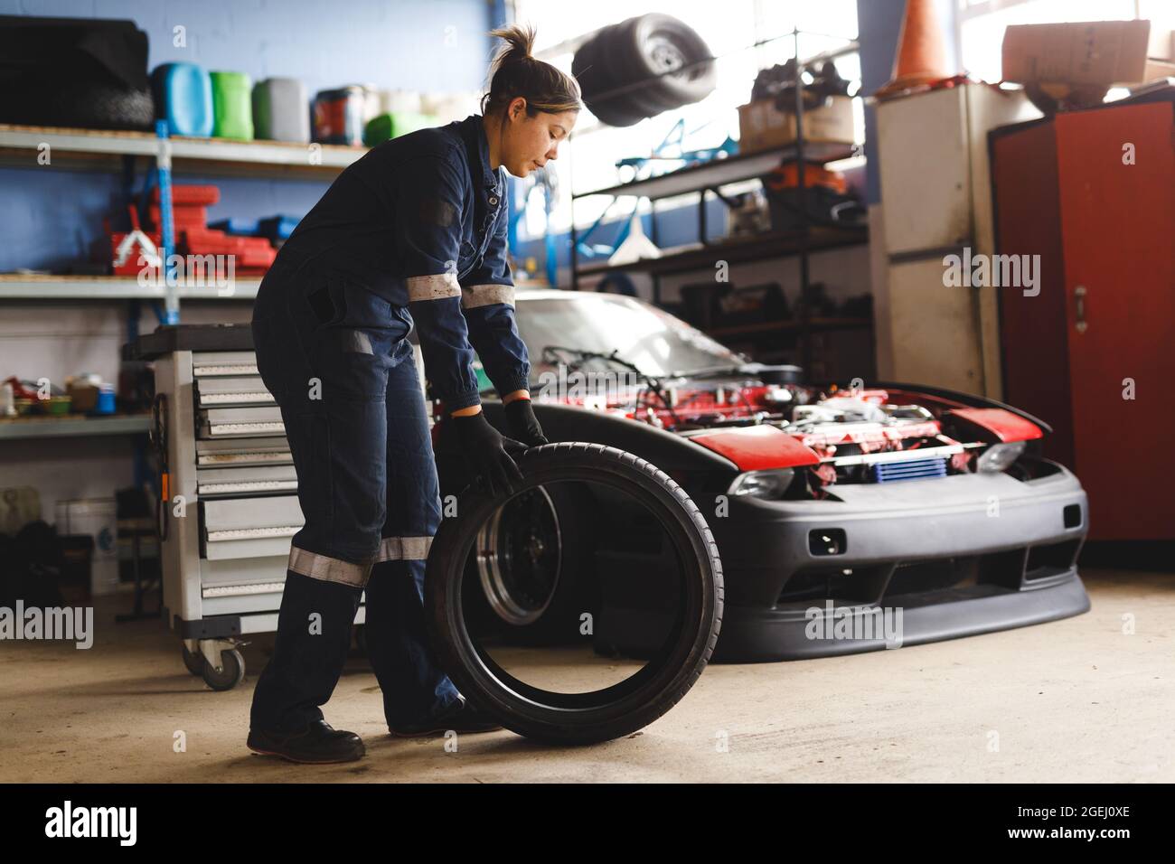 Mixed race female car mechanic wearing overalls, holding tire Stock ...