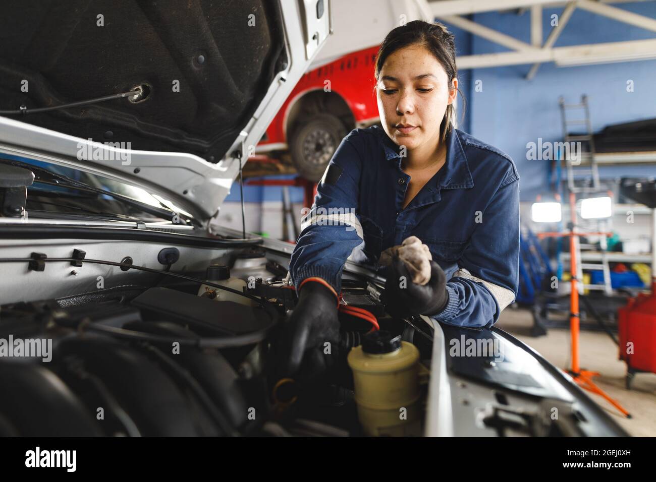 Mixed race female car mechanic wearing overalls, checking oil level ...