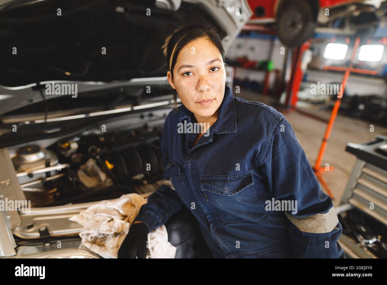 Mixed race female car mechanic wearing overalls, inspecting car and ...