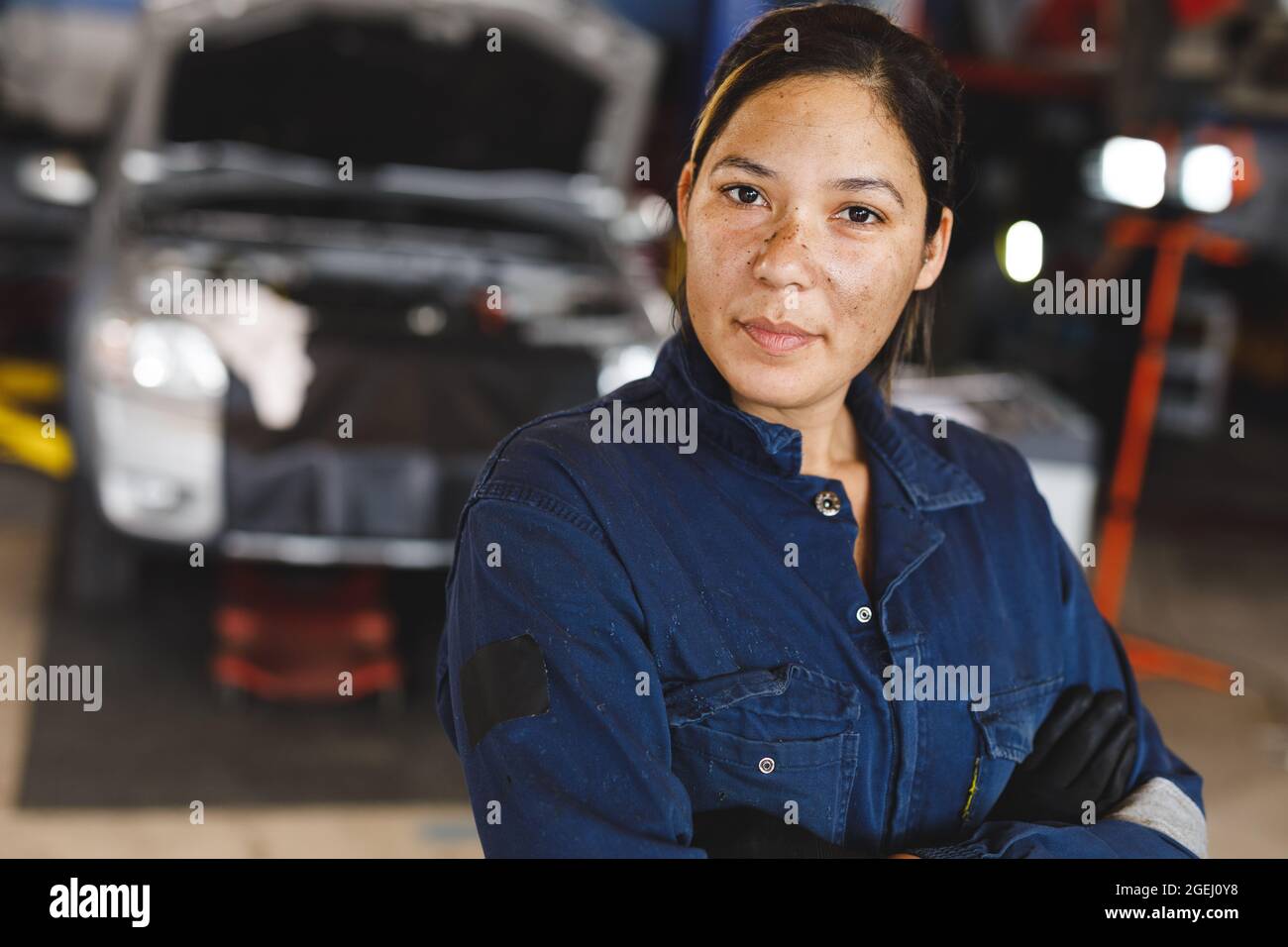 Mixed race female car mechanic wearing overalls, looking at camera ...