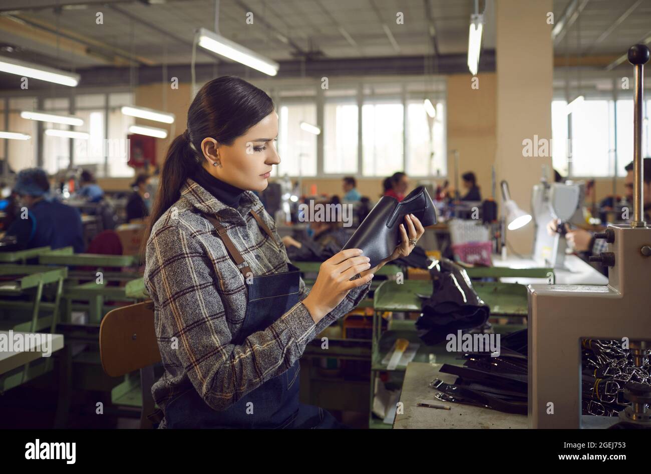Woman making new leather boots standing at a table in a workshop of a ...