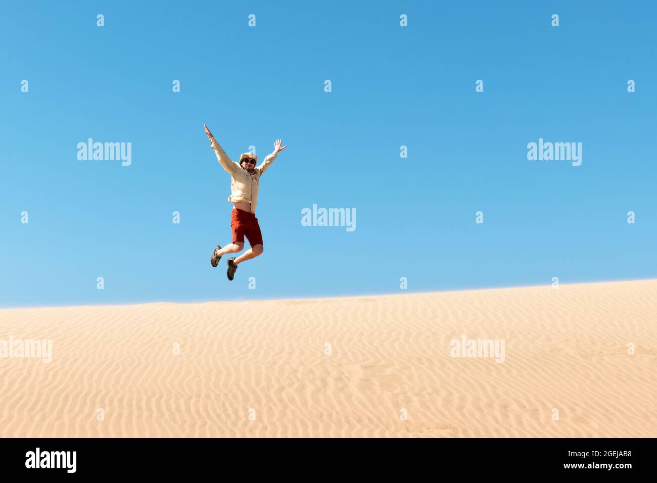 Single man jump on sand in the Namib desert at sunrise on blue sky ...