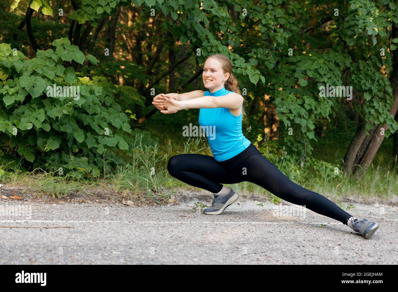 Young girl doing warm-up and stretching legs on alleyway in the park ...