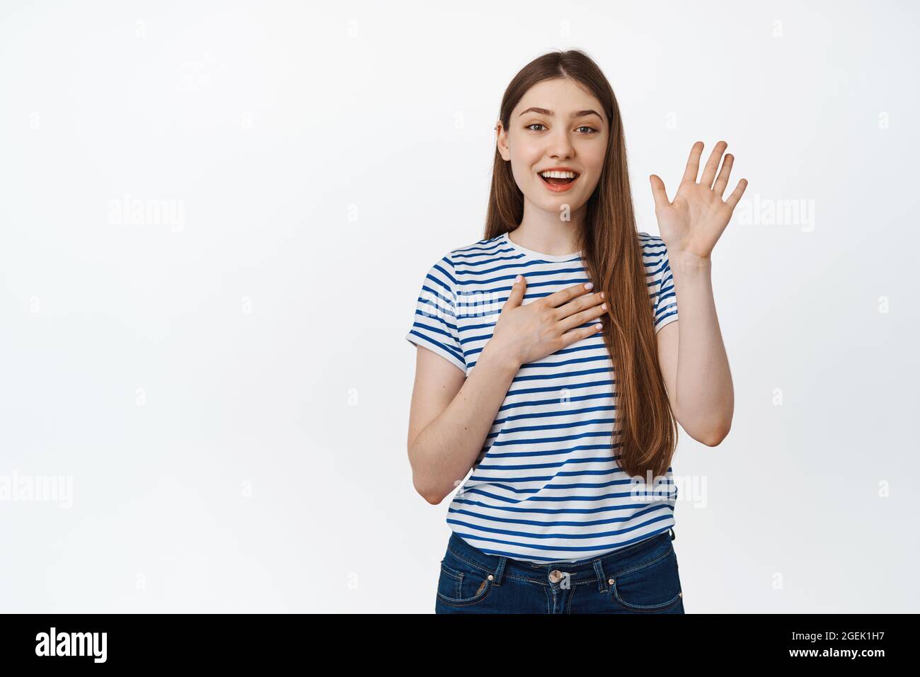 Young friendly girl smiling, raising one hand, put arm on heart ...