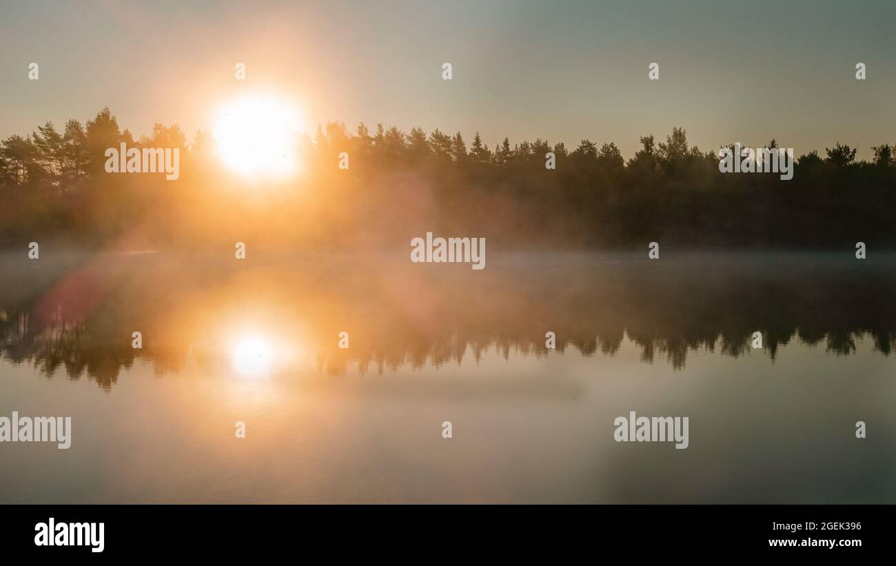 Scenic misty glowing sunrise over lake with large orange Sun, Sun rays ...