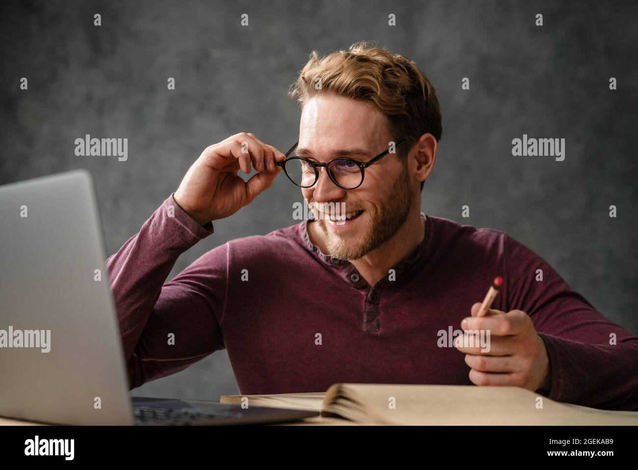 The smiling man looking into laptop screen and adjusting glasses while ...