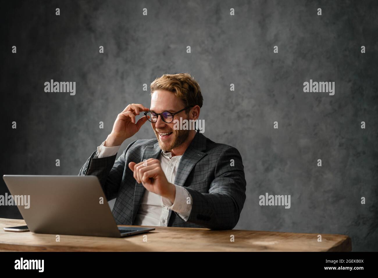 The smiling man in glasses and jacket looking into laptop screen while ...