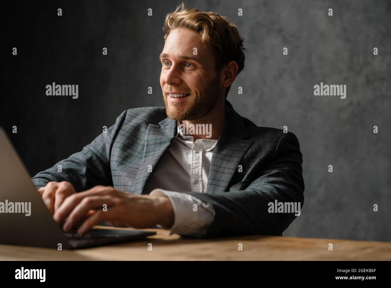 The portrait of smiling man typing on laptop while sitting at the table ...