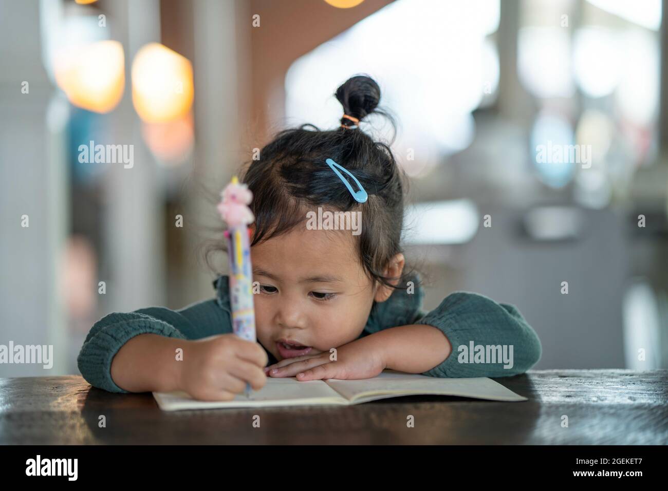 Beautiful Southeast Asian female kid writing something in her copybook ...