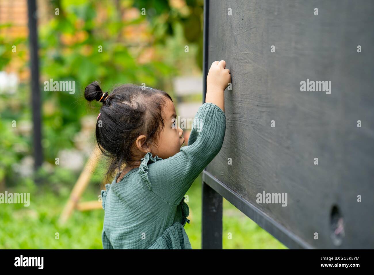 Beautiful Southeast Asian female kid writing something on a blackboard ...