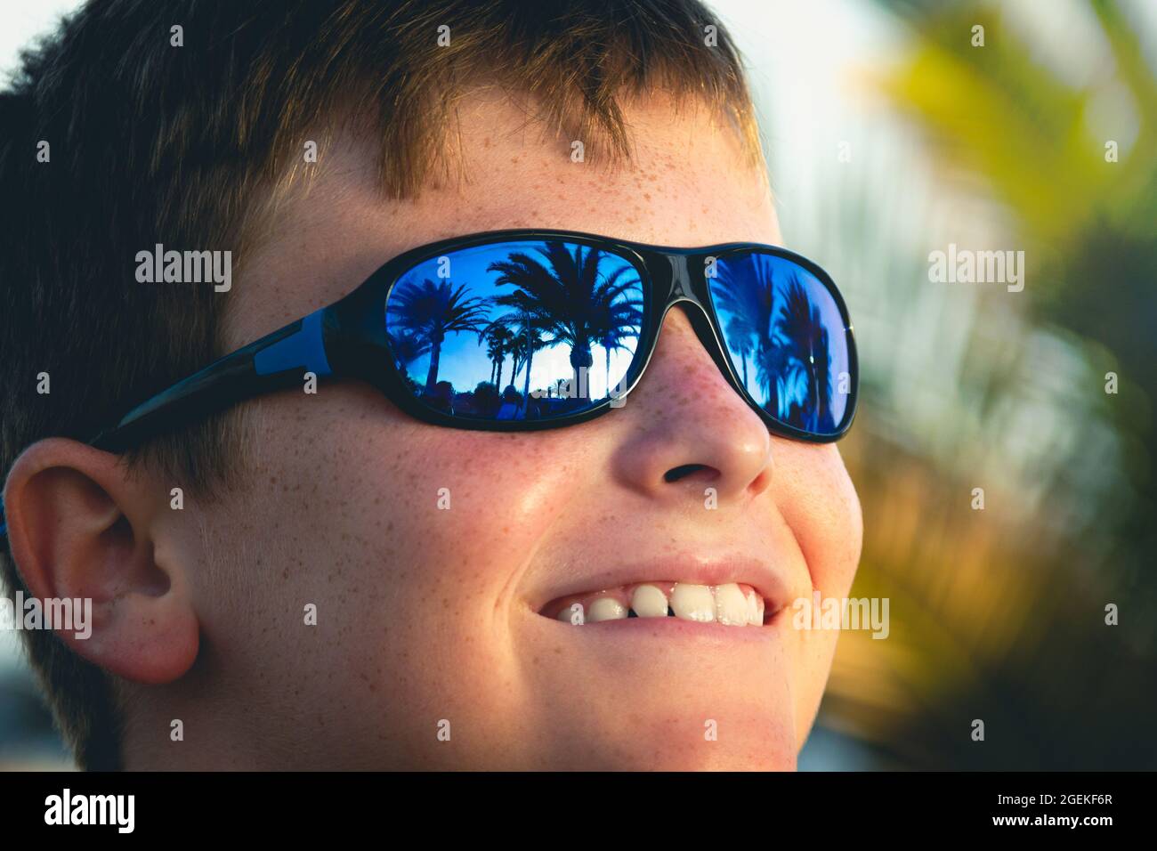 Smiling little boy with blue sunglasses at sunny day outdoors. Palm ...