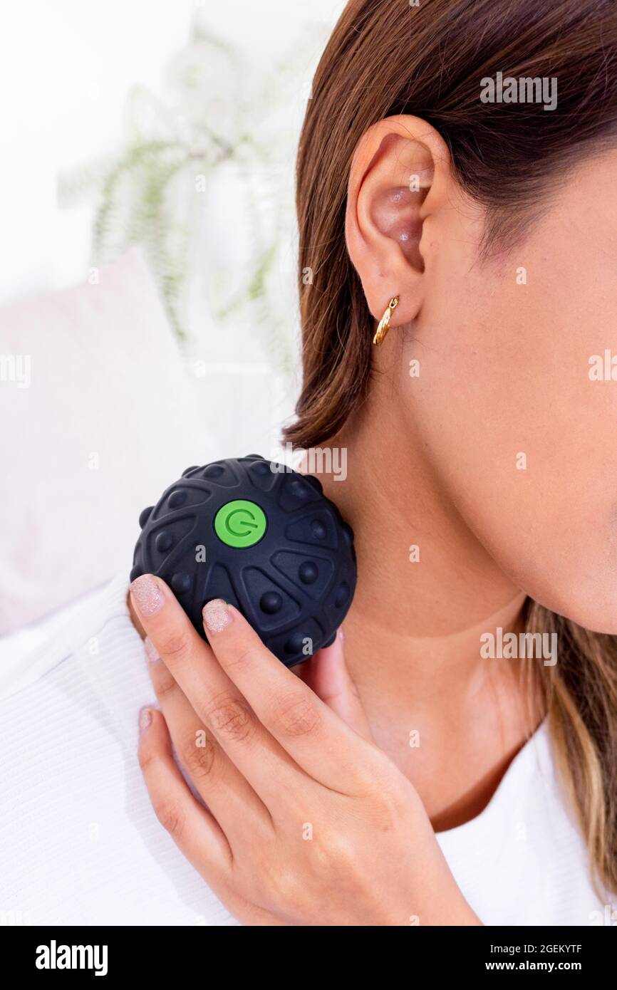 Vertical shot of a woman massaging her neck by the mini vibrating hand ...