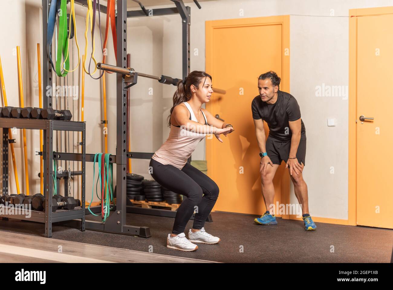 Young woman doing squats without weighting exercise with trainer in gym ...