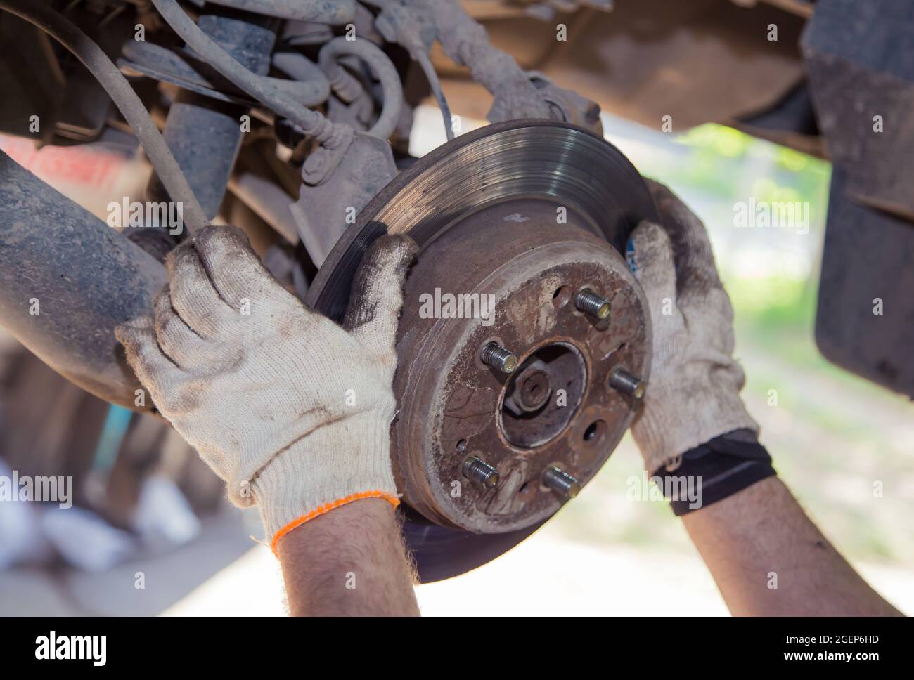 The man's hands remove the worn brake disc from the rear wheel hub. In ...