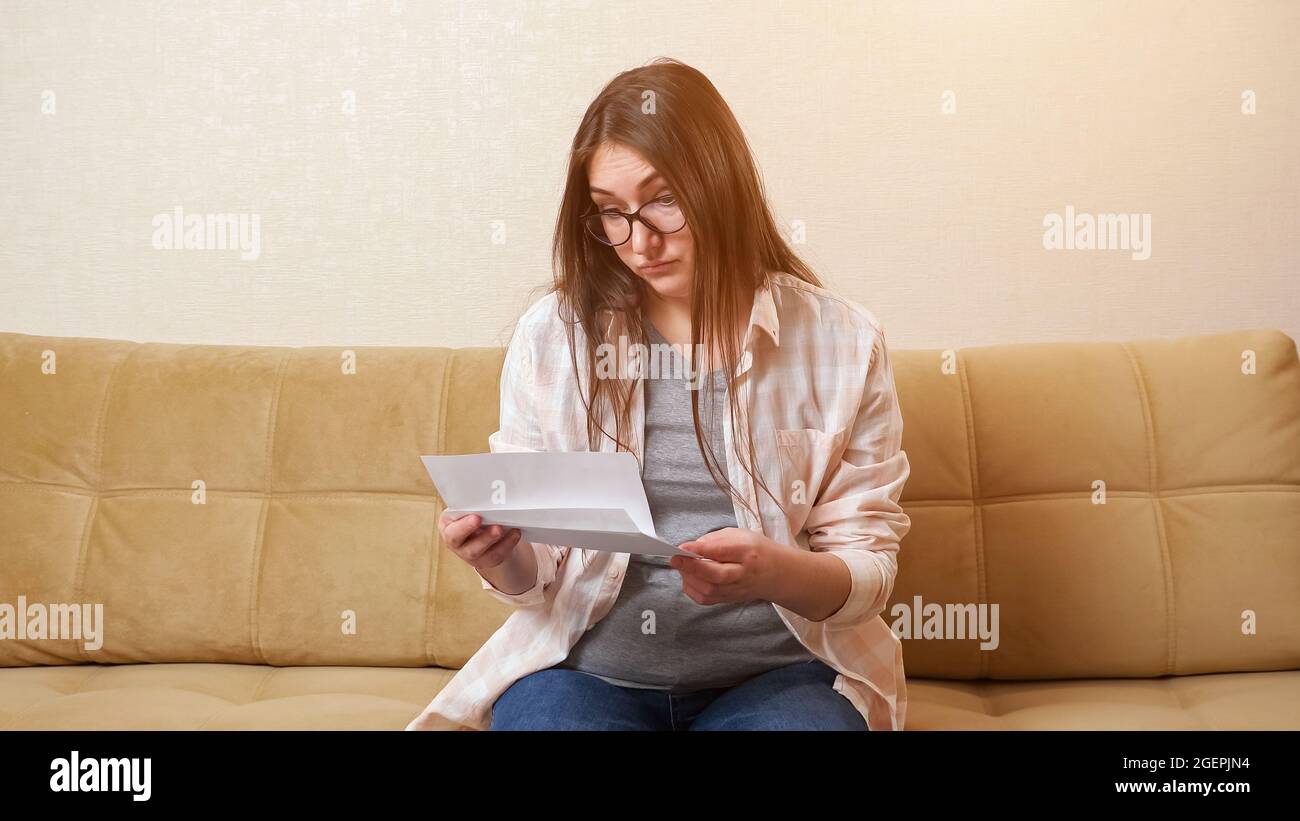 Woman opens envelope with bill and becomes nervous on couch Stock Photo ...