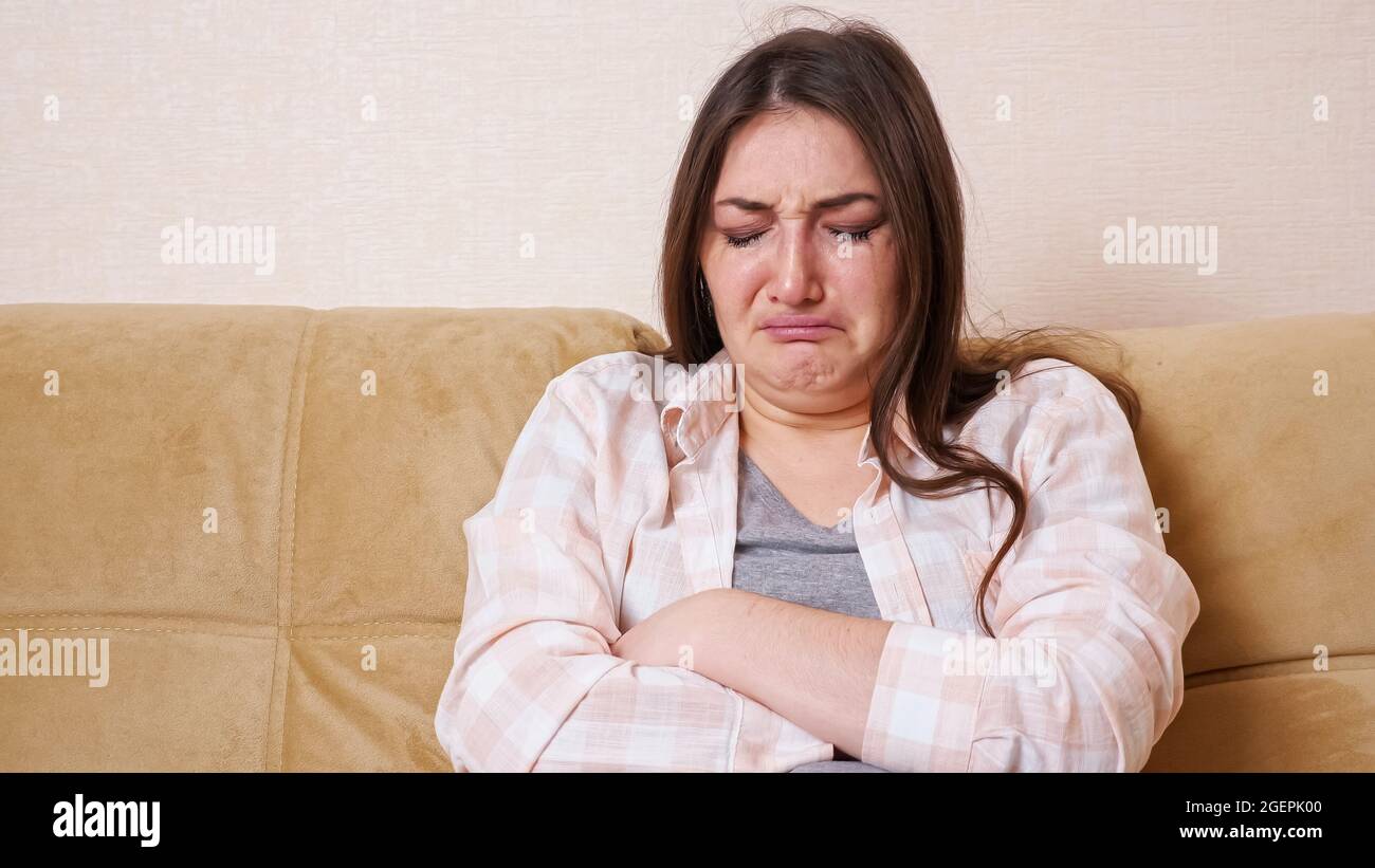 Young brunette woman crying sitting on the sofa Stock Photo - Alamy