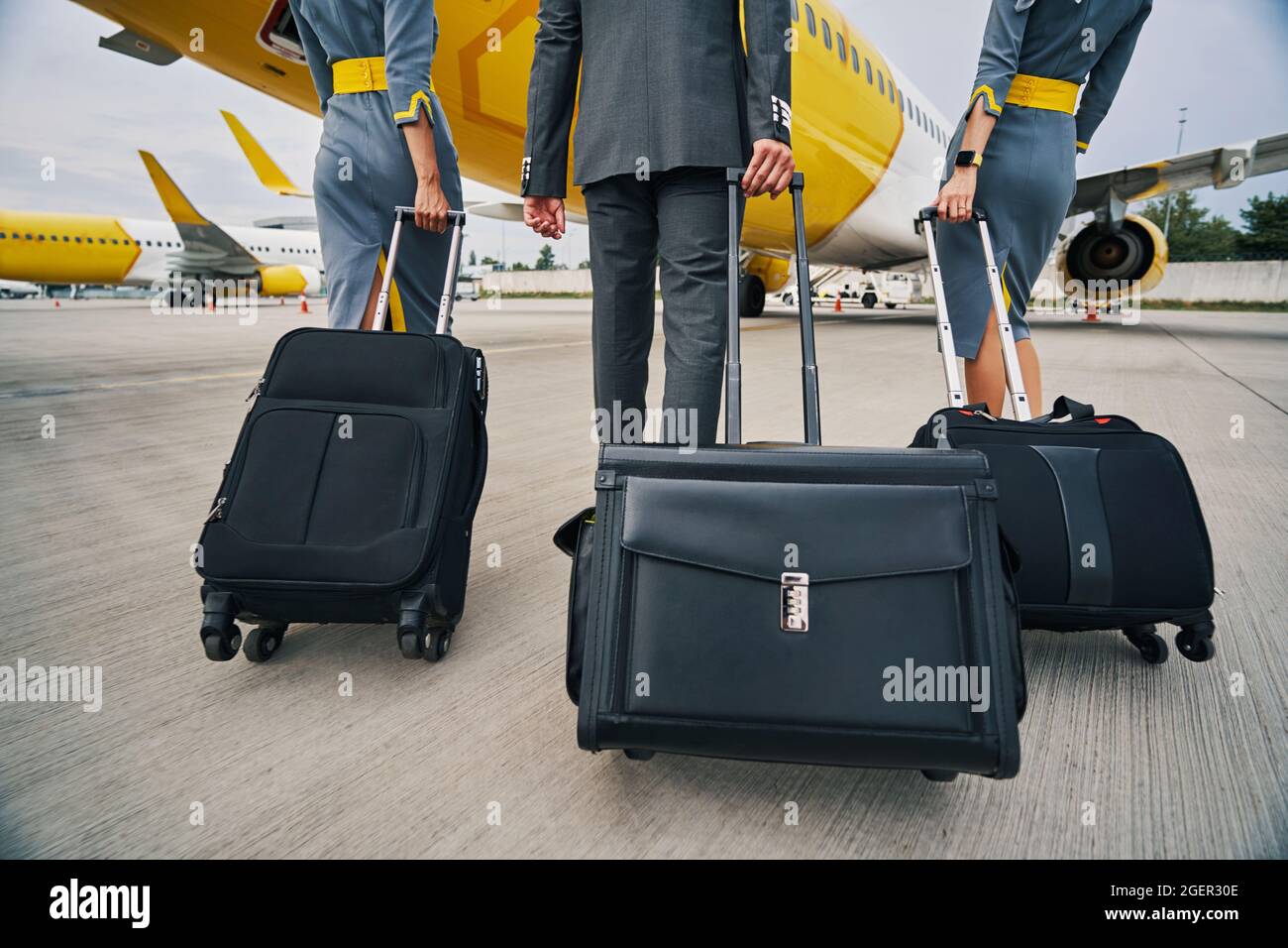 Pilot and stewardesses with luggage walking towards the landed aircraft ...