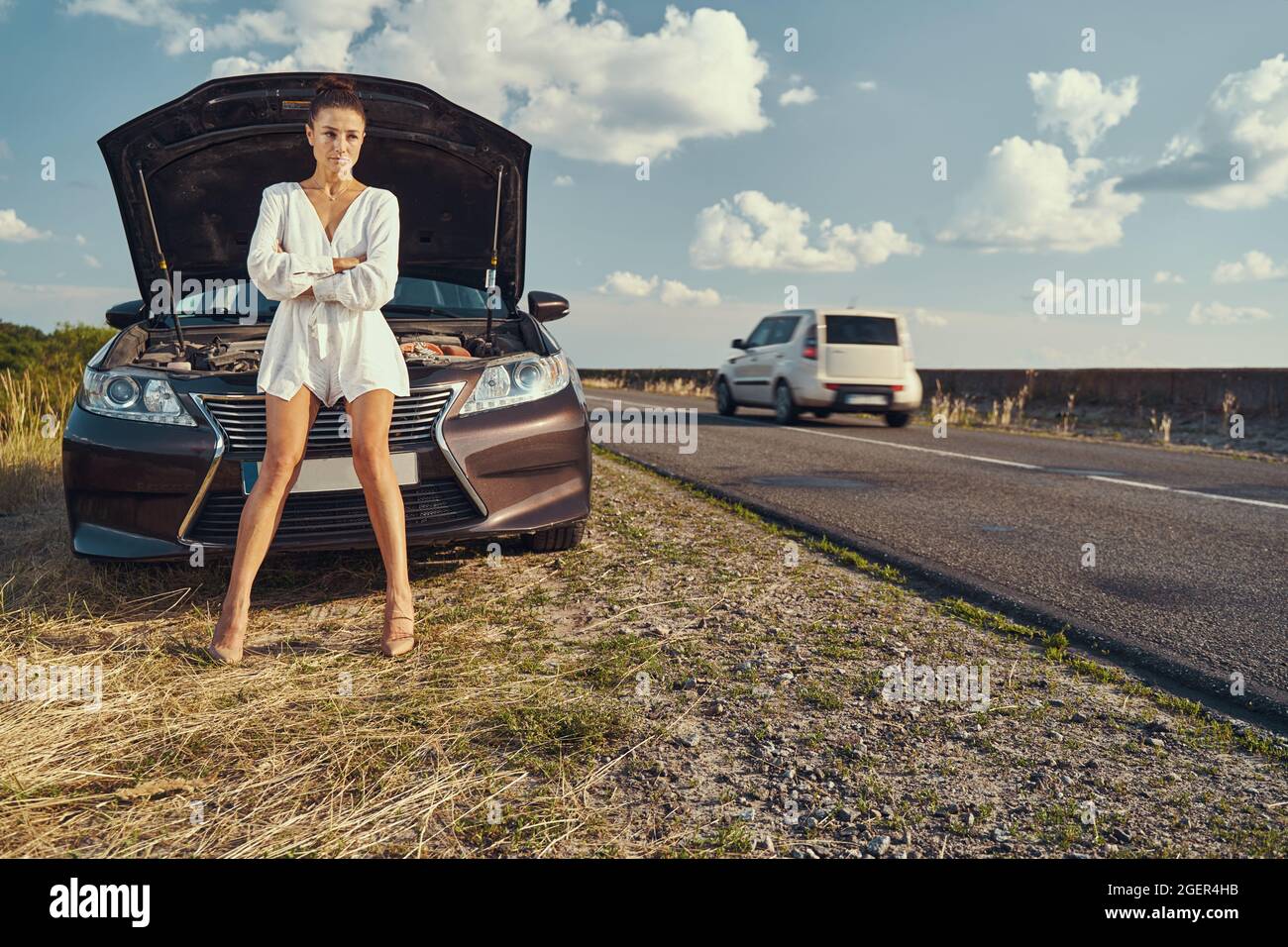 Annoyed woman leaning against broken car with crossed arms Stock Photo ...