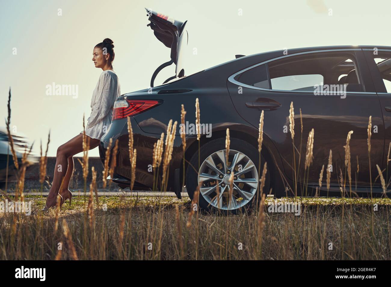 Desperate female leaning against the car trunk Stock Photo - Alamy