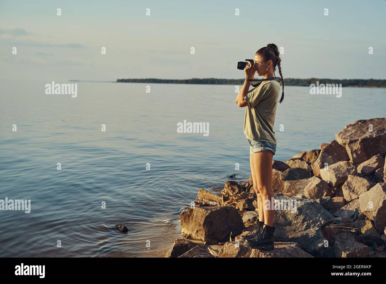 Lean lady on river bank taking photos of water surface Stock Photo - Alamy