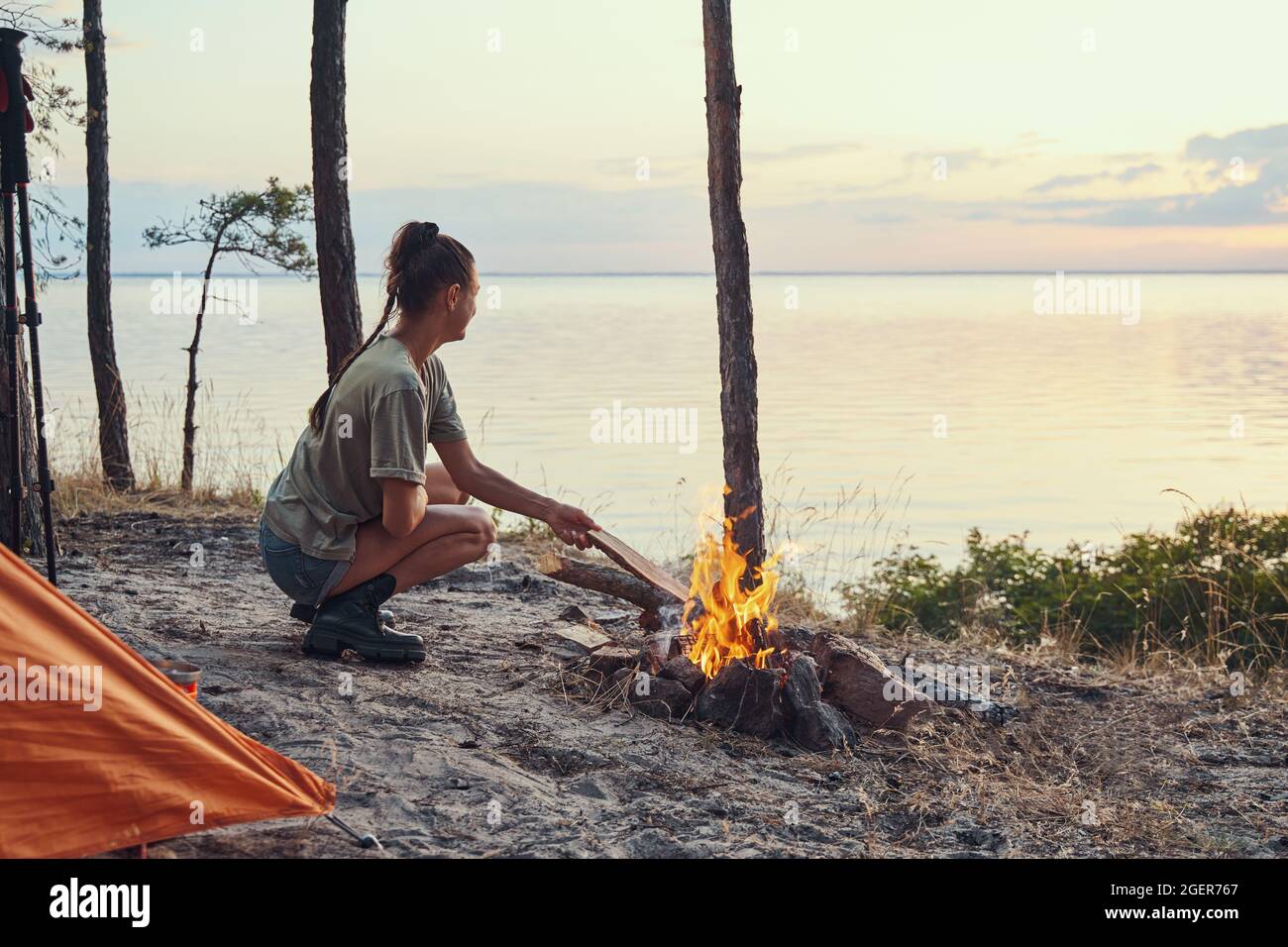 Camper adding wooden fuel to fire in nature Stock Photo - Alamy